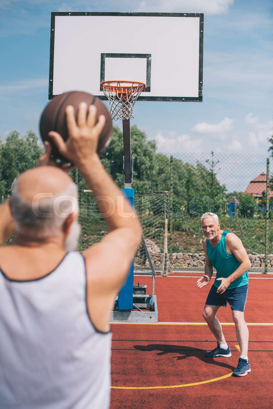elderly men playing basketball together on playground on summer day ...