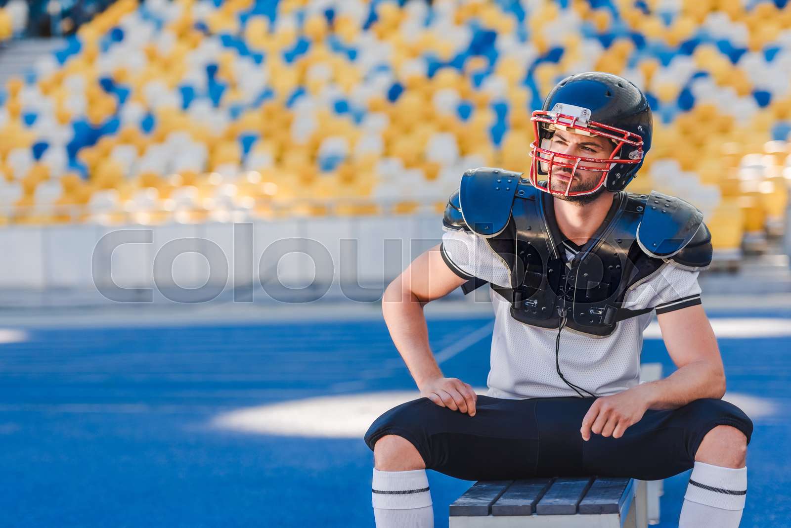 handsome young american football player sitting on bench at sports ...