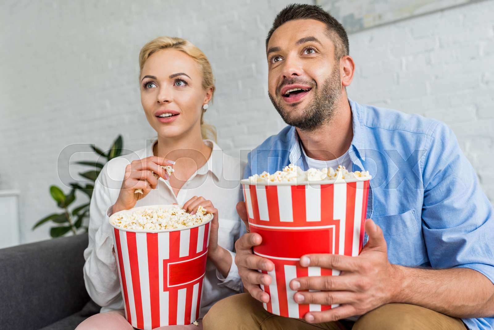excited couple eating popcorn and looking away at home | Stock image ...