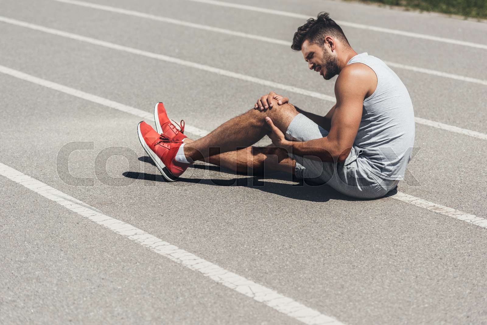 young runner with leg injury sitting on floor of running track | Stock ...