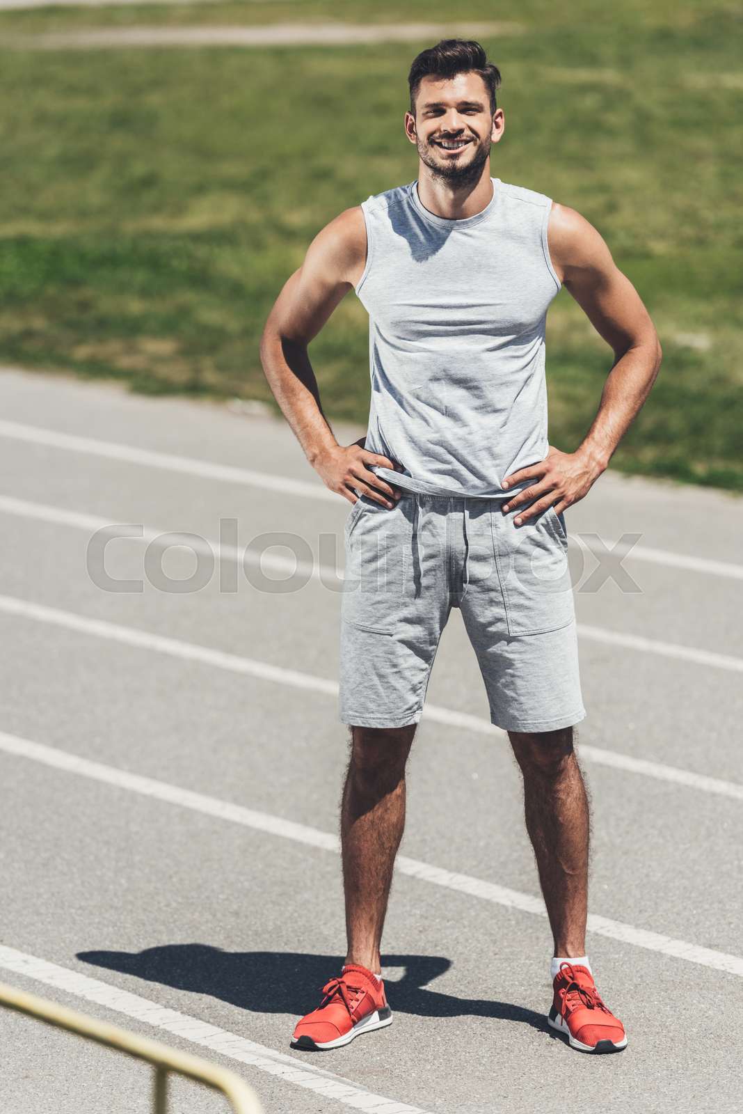 happy young man standing on running track with arms akimbo | Stock ...