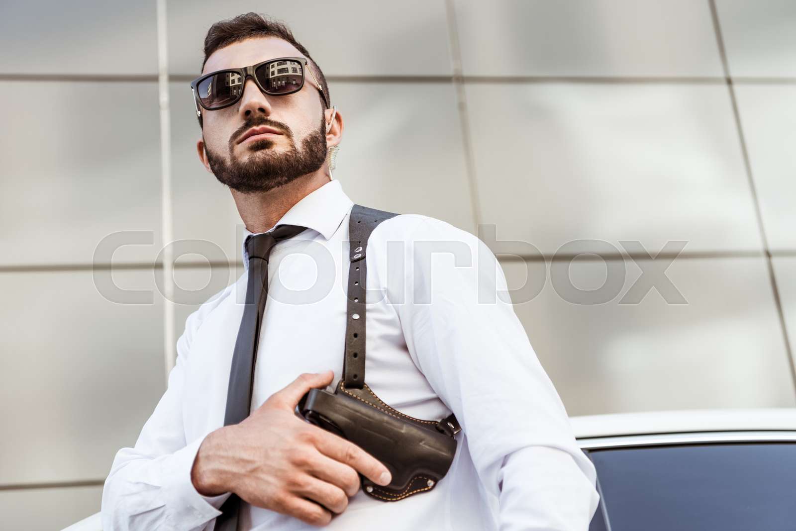 low angle view of handsome security guard in sunglasses touching gun ...