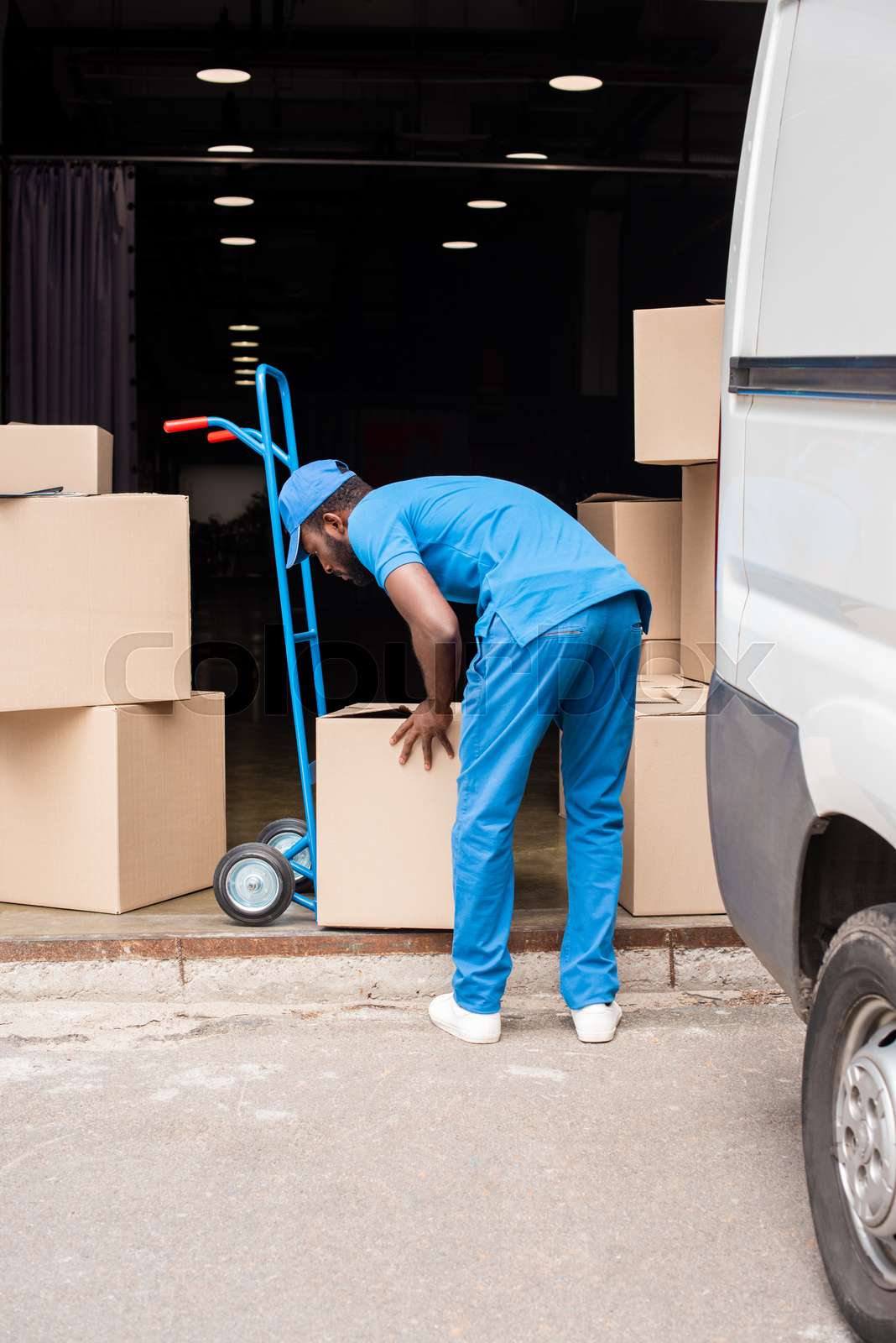 side view of african american delivery man putting boxes on cart ...