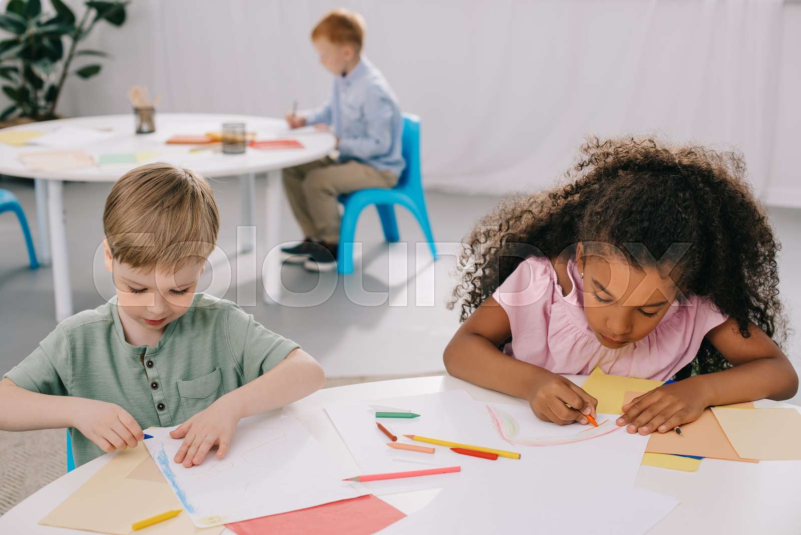 multicultural preschoolers drawing pictures with pencils in classroom ...