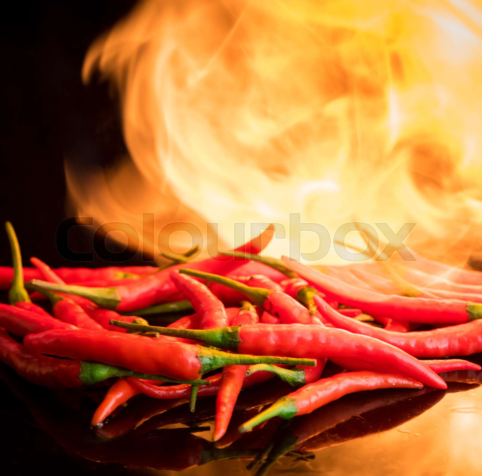 Hot chilli with burning fire on black surface | Stock image | Colourbox