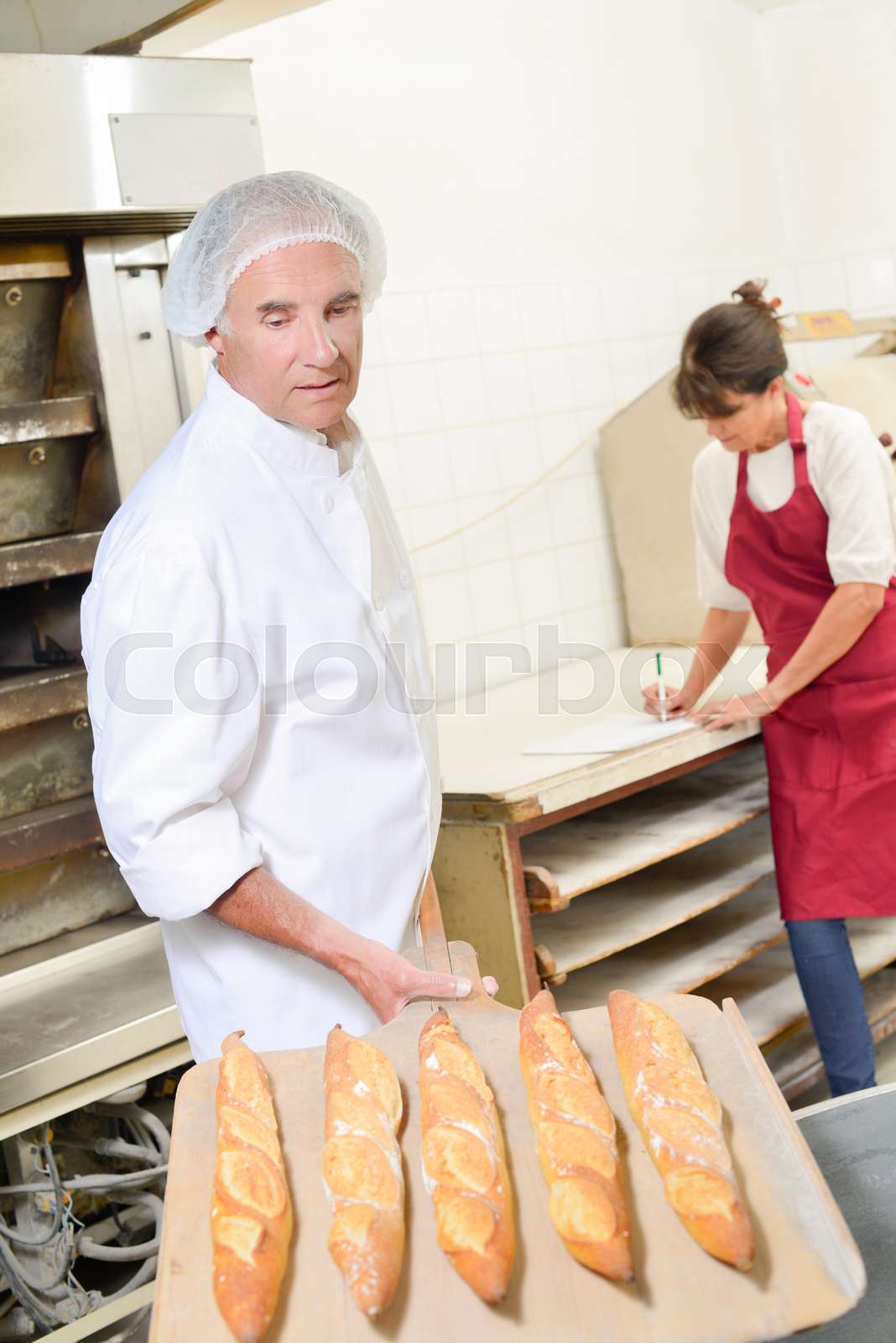 Baker holding five baguettes on a peel | Stock image | Colourbox