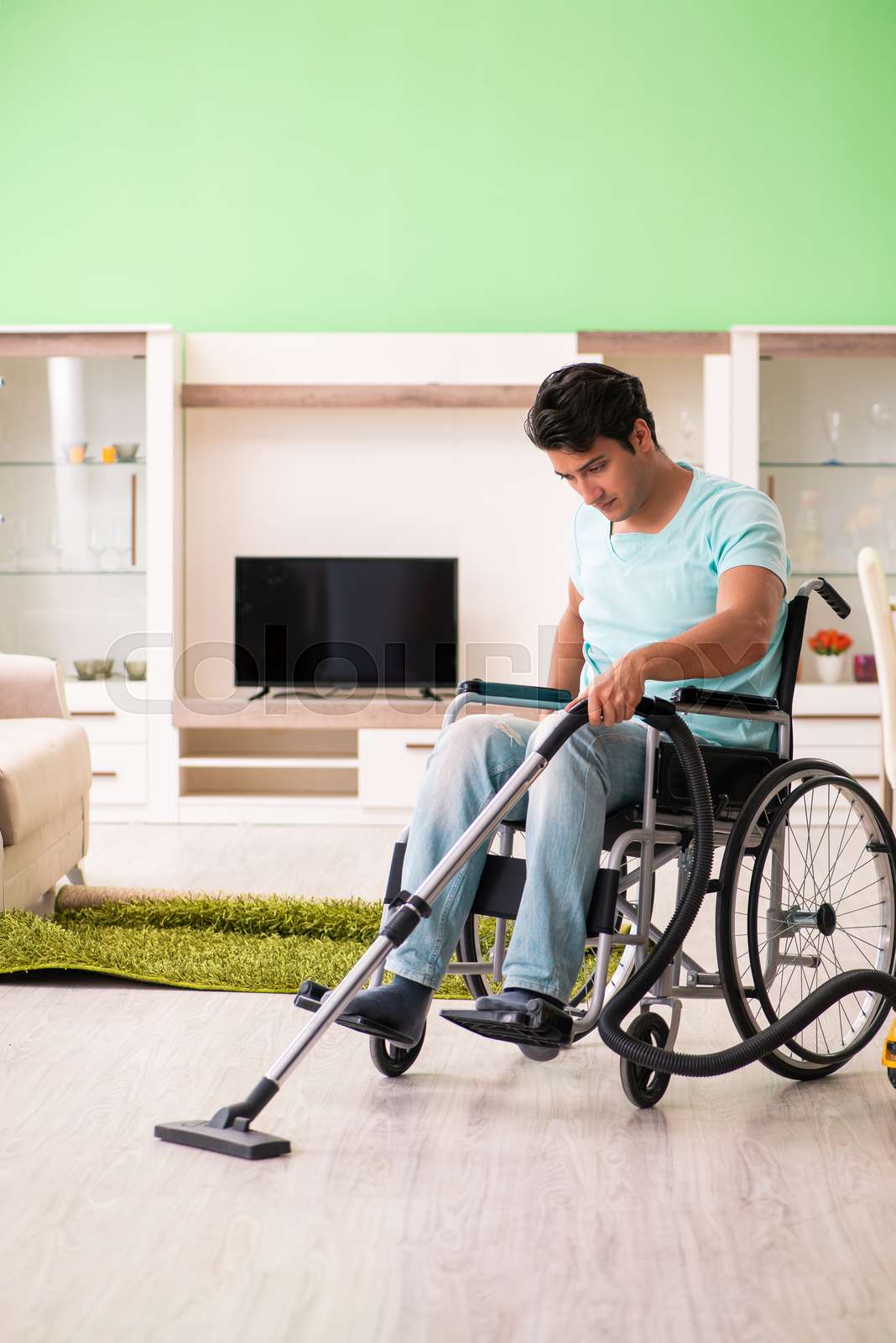 Disabled man on wheelchair vacuum cleaning house | Stock image | Colourbox