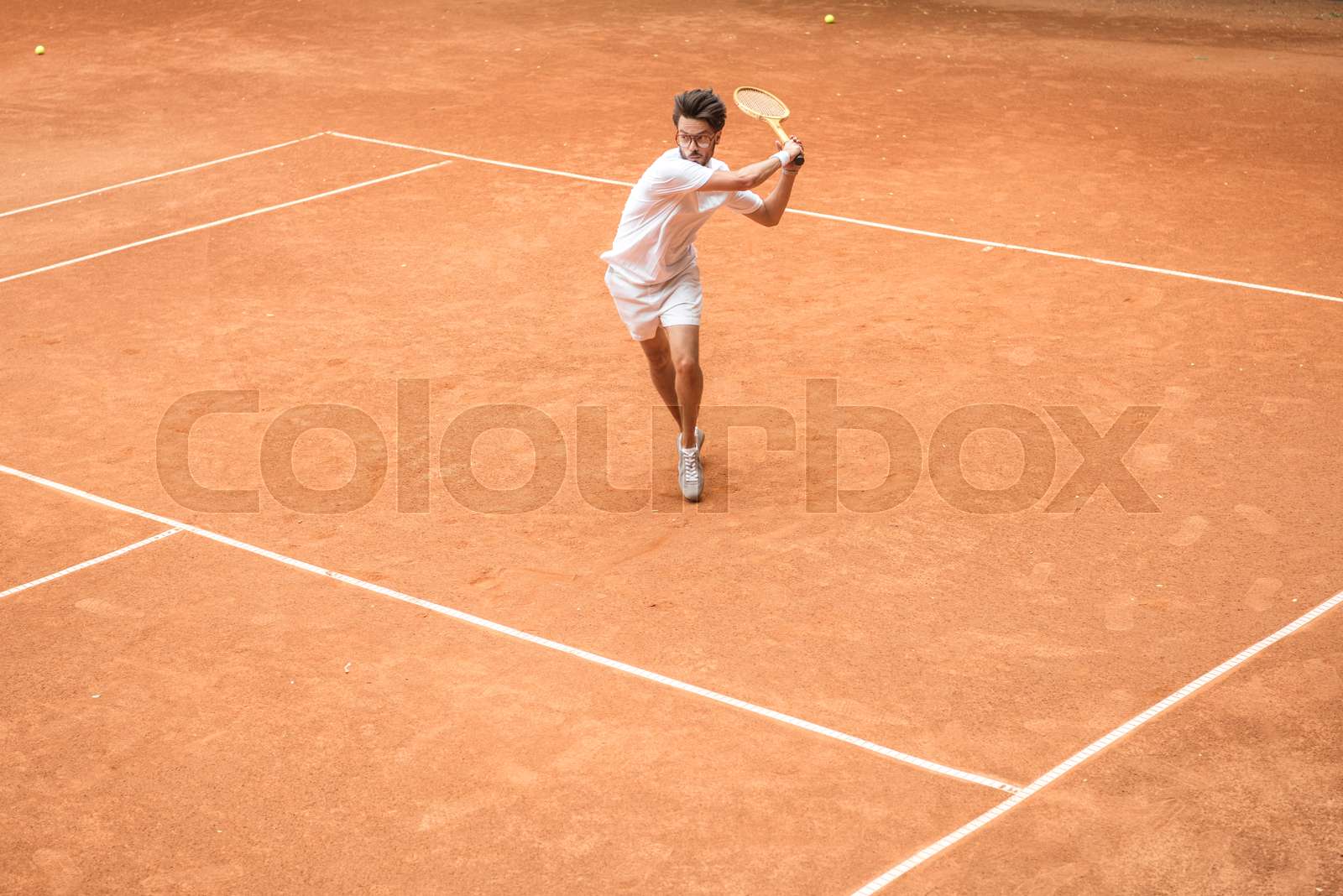 old-fashioned tennis player training with wooden racket on brown court ...