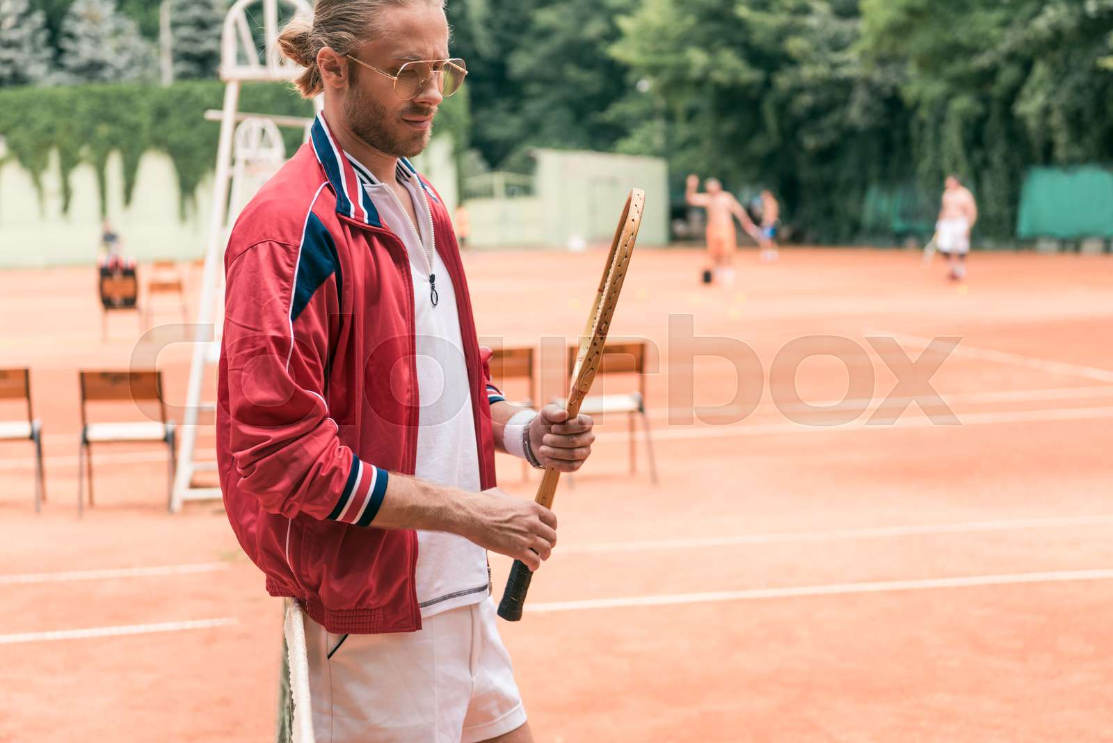 handsome old-fashioned tennis player with wooden racket standing at net ...