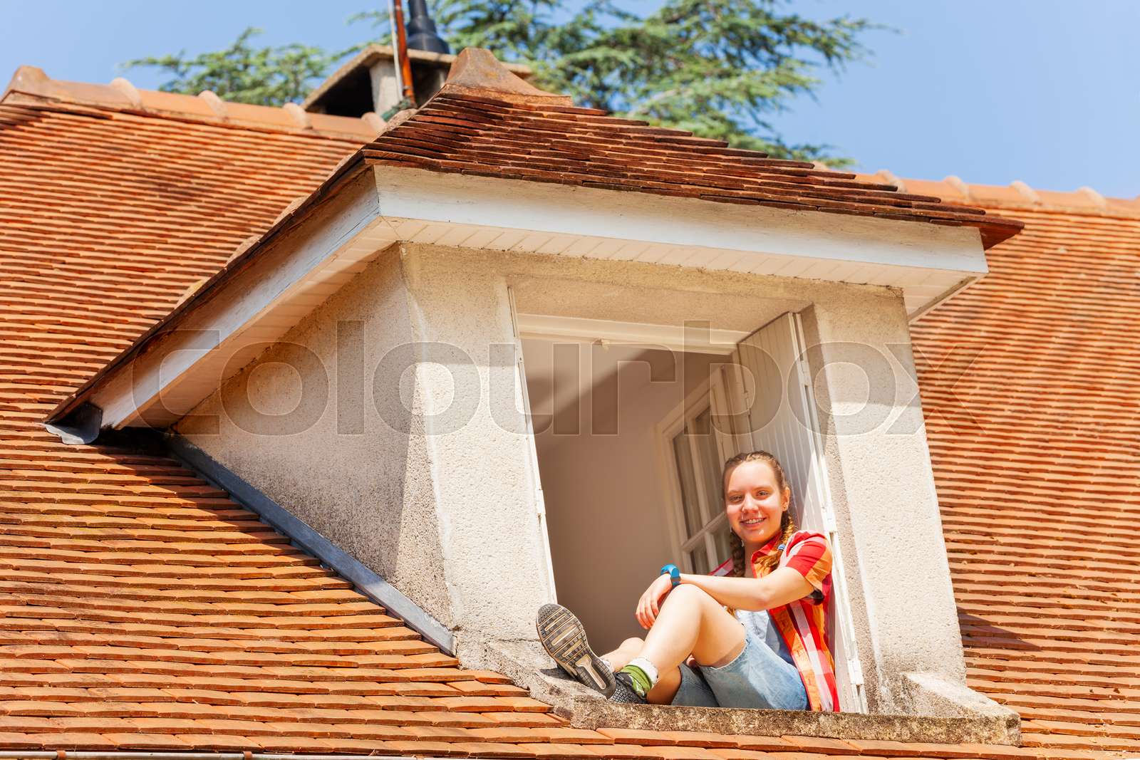 Girl looking down to street from open attic window | Stock image ...