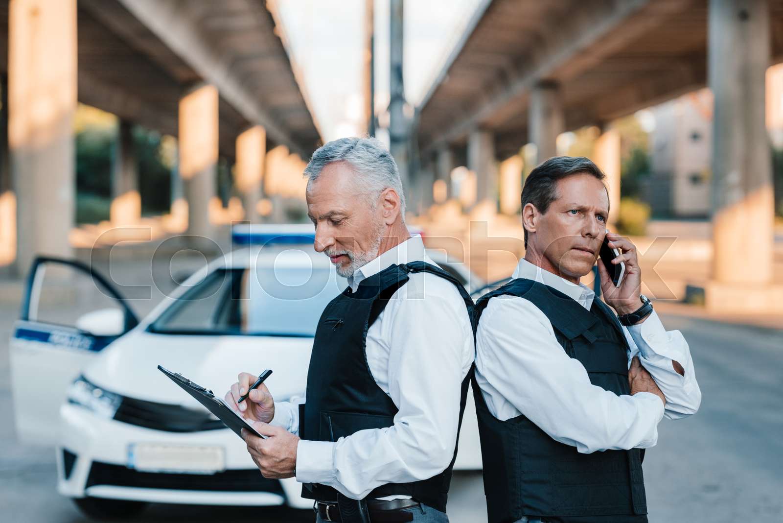 mature police officer talking on smartphone and standing with colleague ...