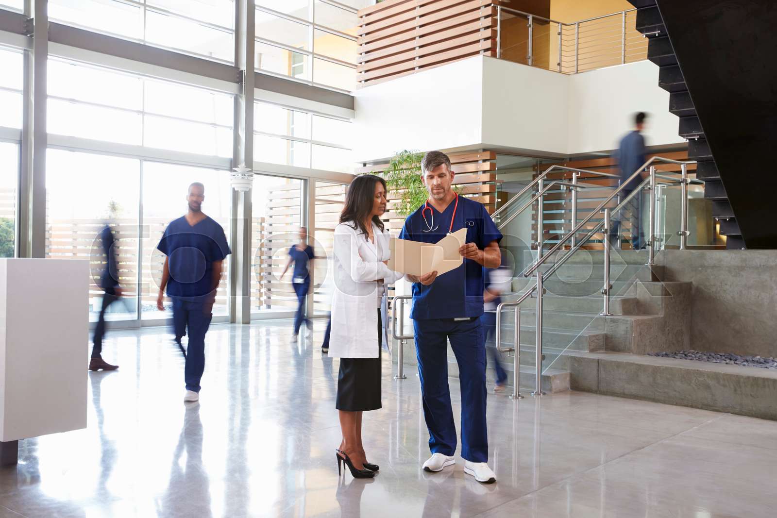 Two healthcare workers talk in the lobby of a busy hospital | Stock ...
