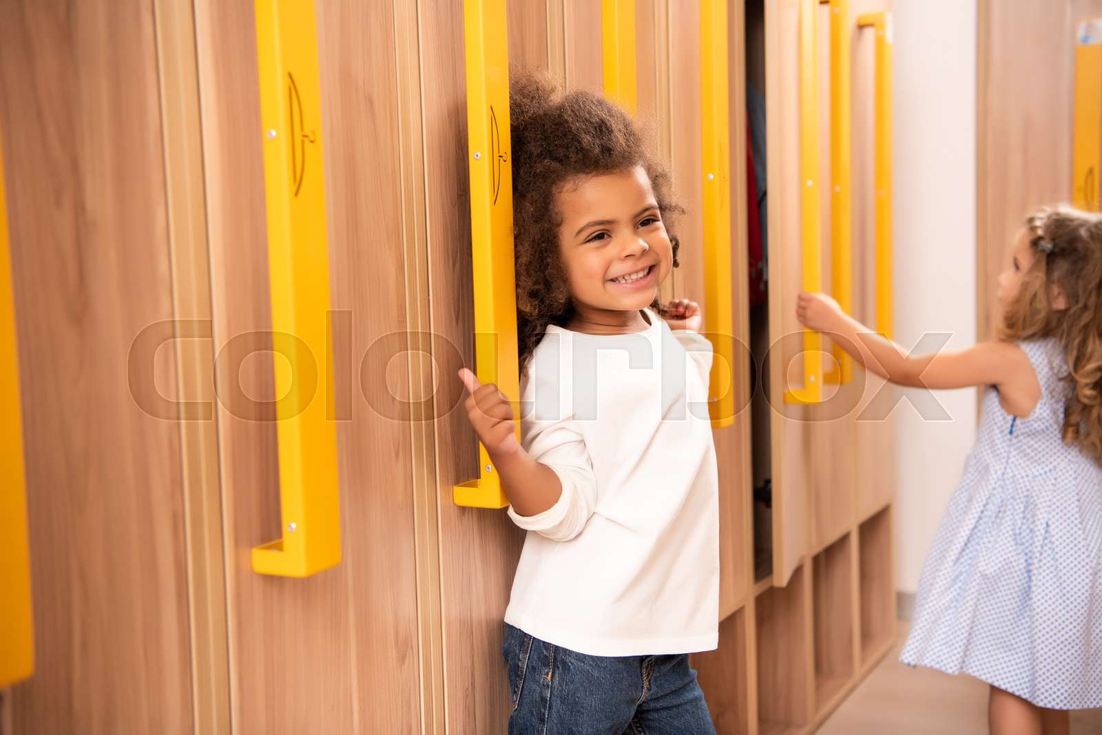 happy multicultural kids standing near lockers in kindergarten ...