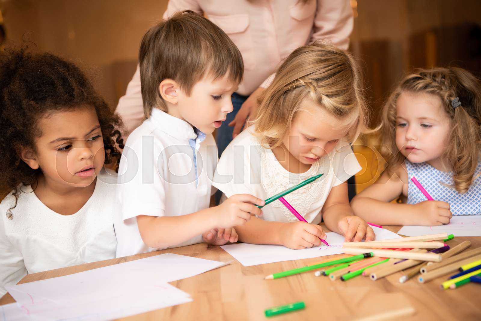 cropped image of educator standing near multicultural kids drawing in ...