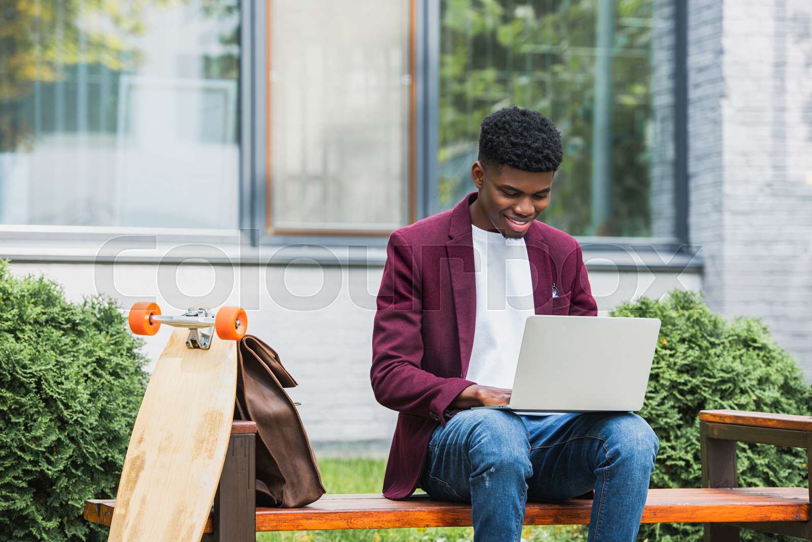 smiling young african american student using laptop on street | Stock ...