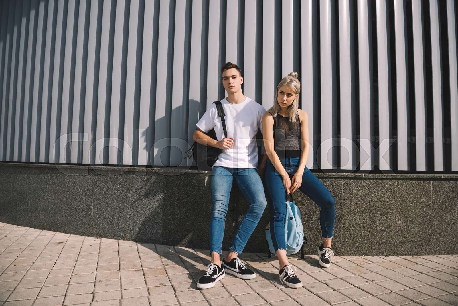 young couple holding backpacks and standing together on street | Stock ...