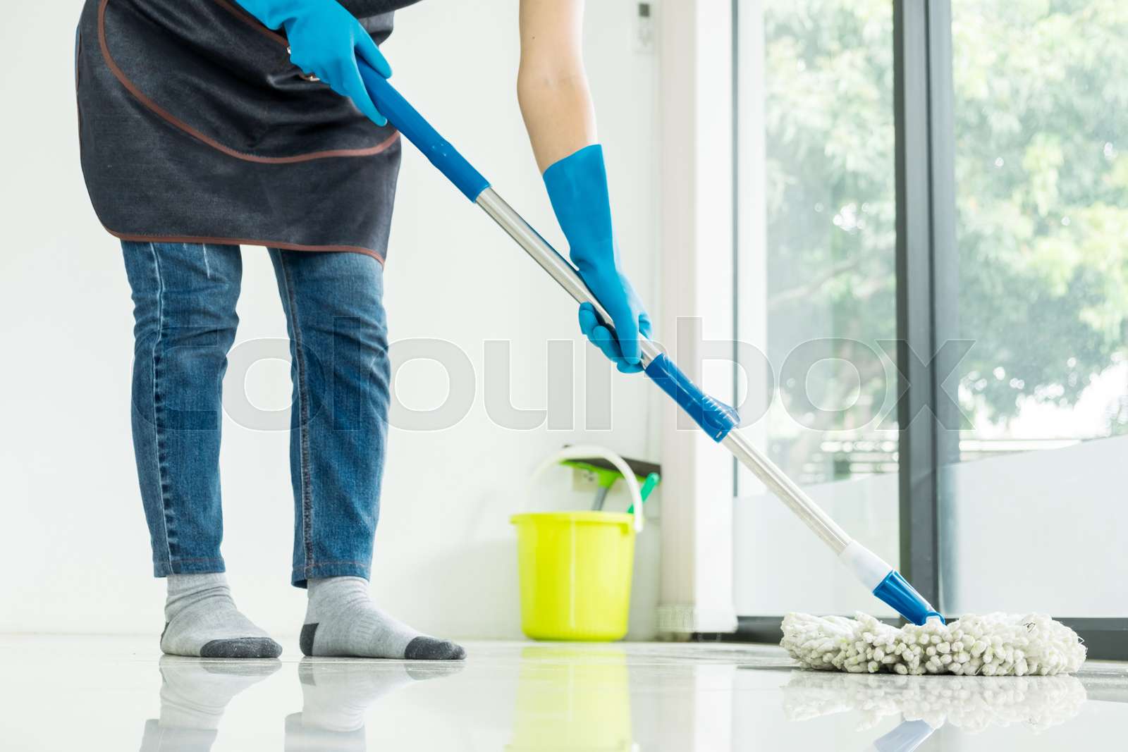 Young housekeeper cleaning floor mobbing holding mop and plastic bucket ...