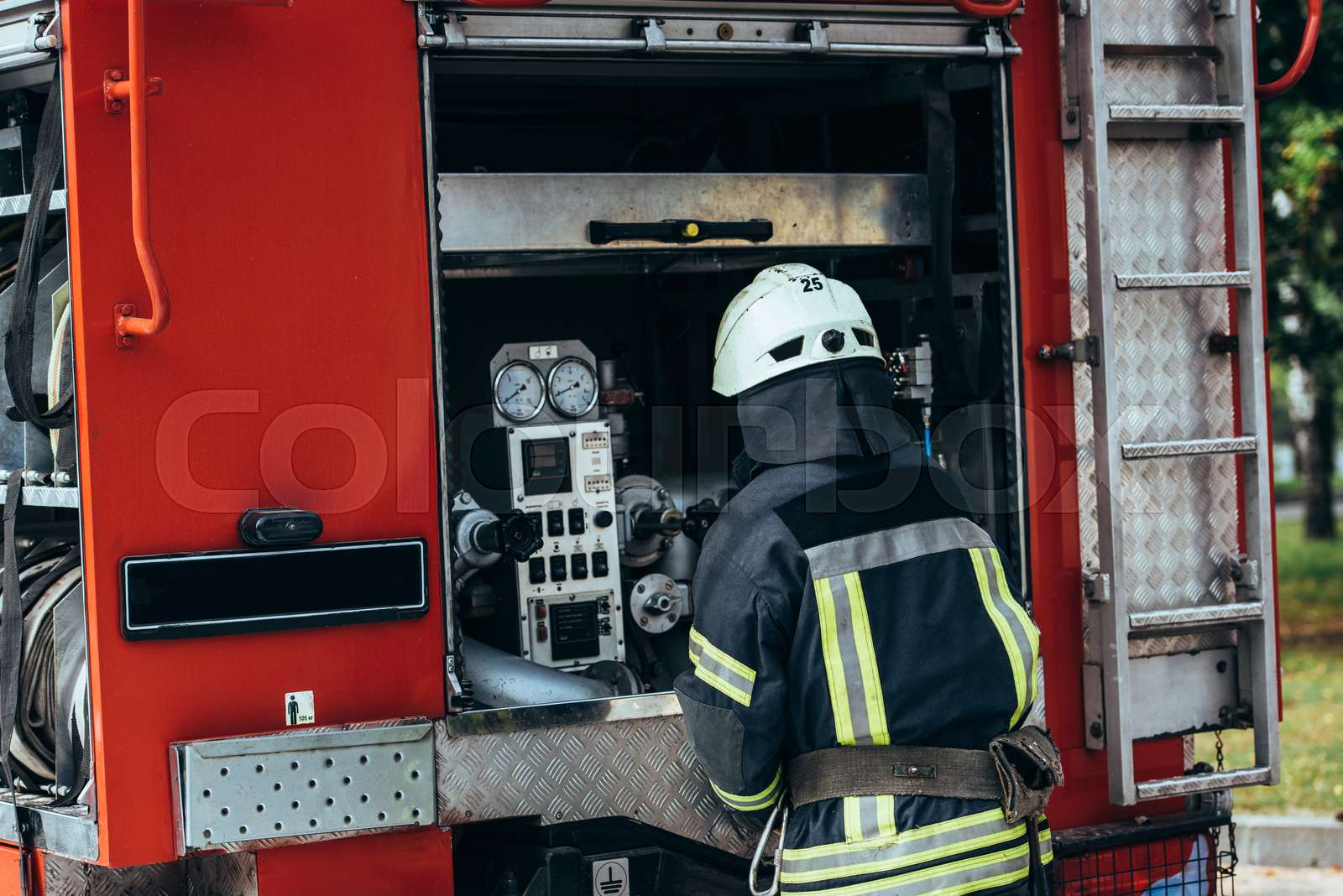 back view of firefighter in uniform and helmet standing at fire truck ...