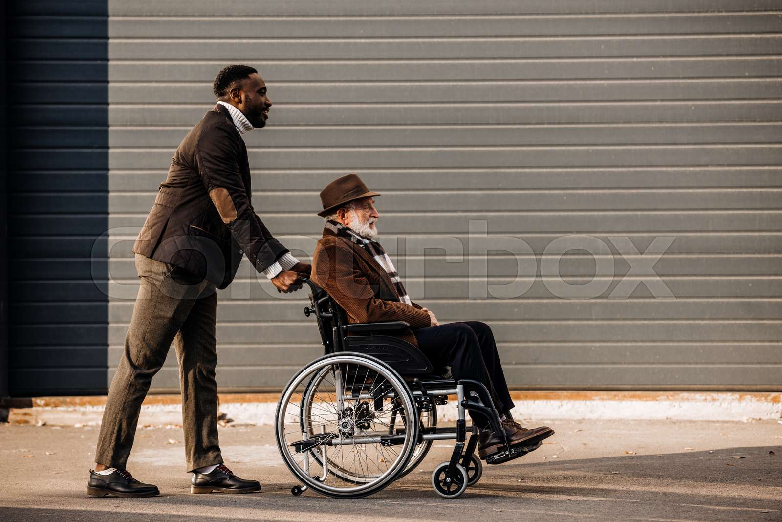 side view of senior disabled man in wheelchair and african american man ...