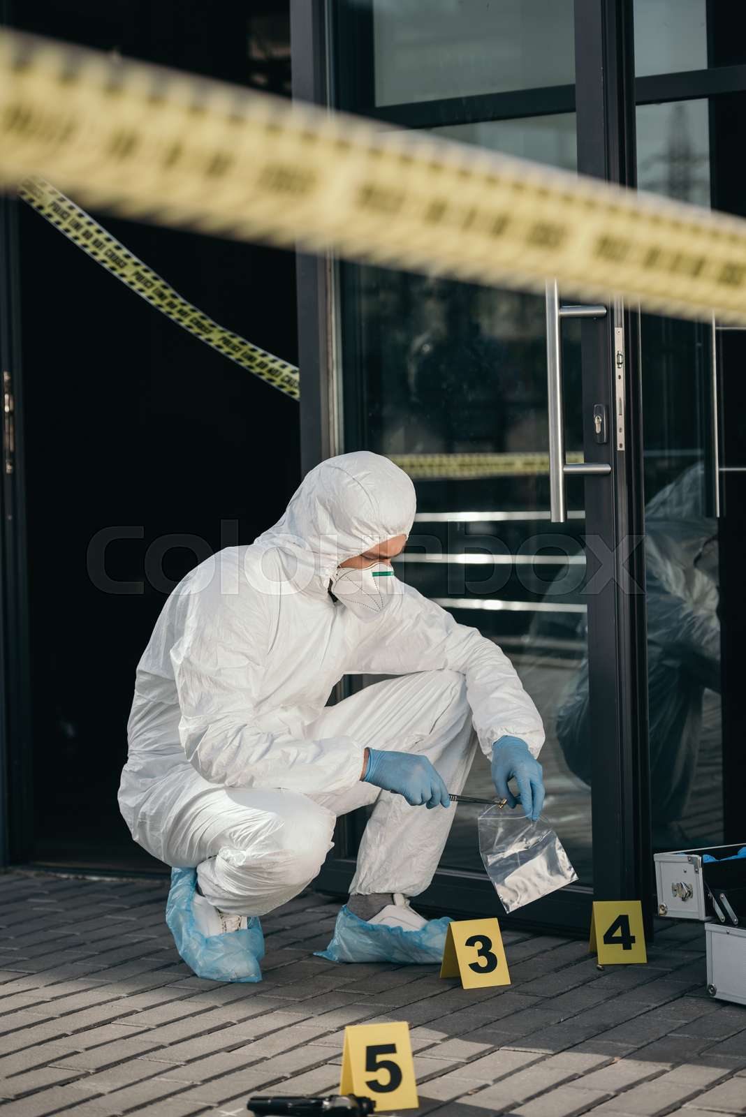 Male Criminologist In Protective Suit And Latex Gloves Packing Evidence