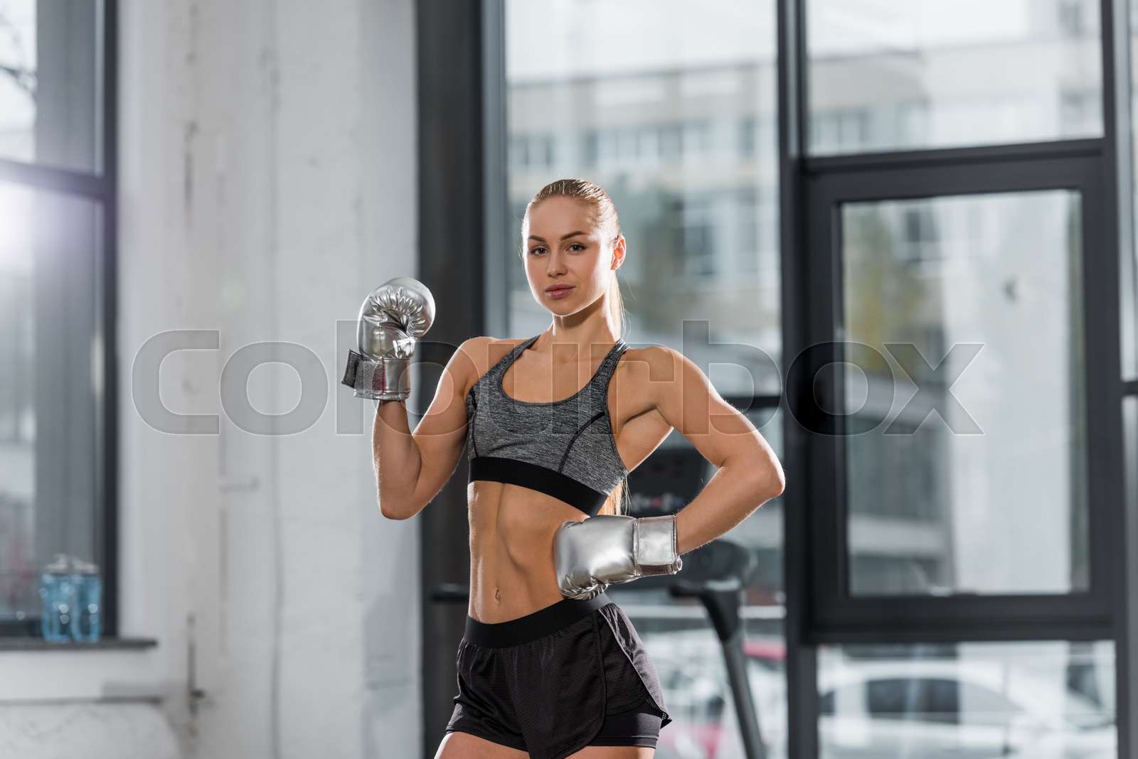 attractive muscular bodybuilder posing with silver boxing gloves in gym ...