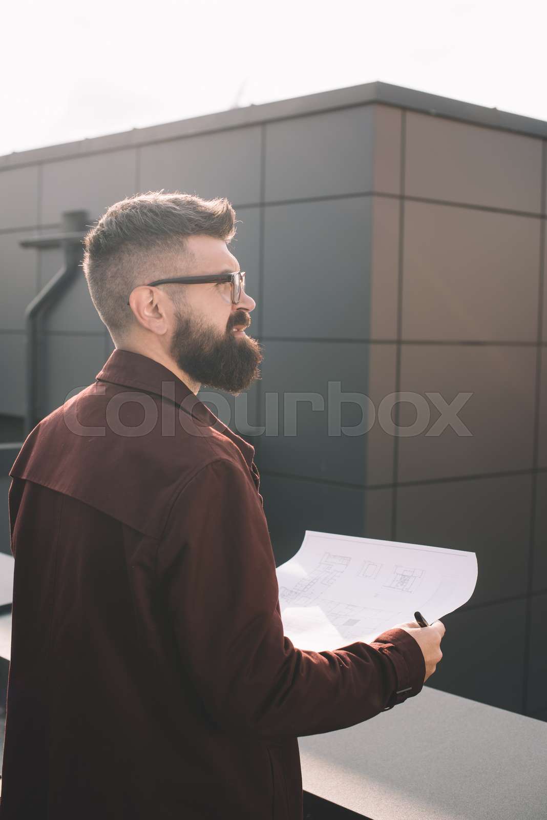 handsome adult male architect in glasses holding blueprint on rooftop ...