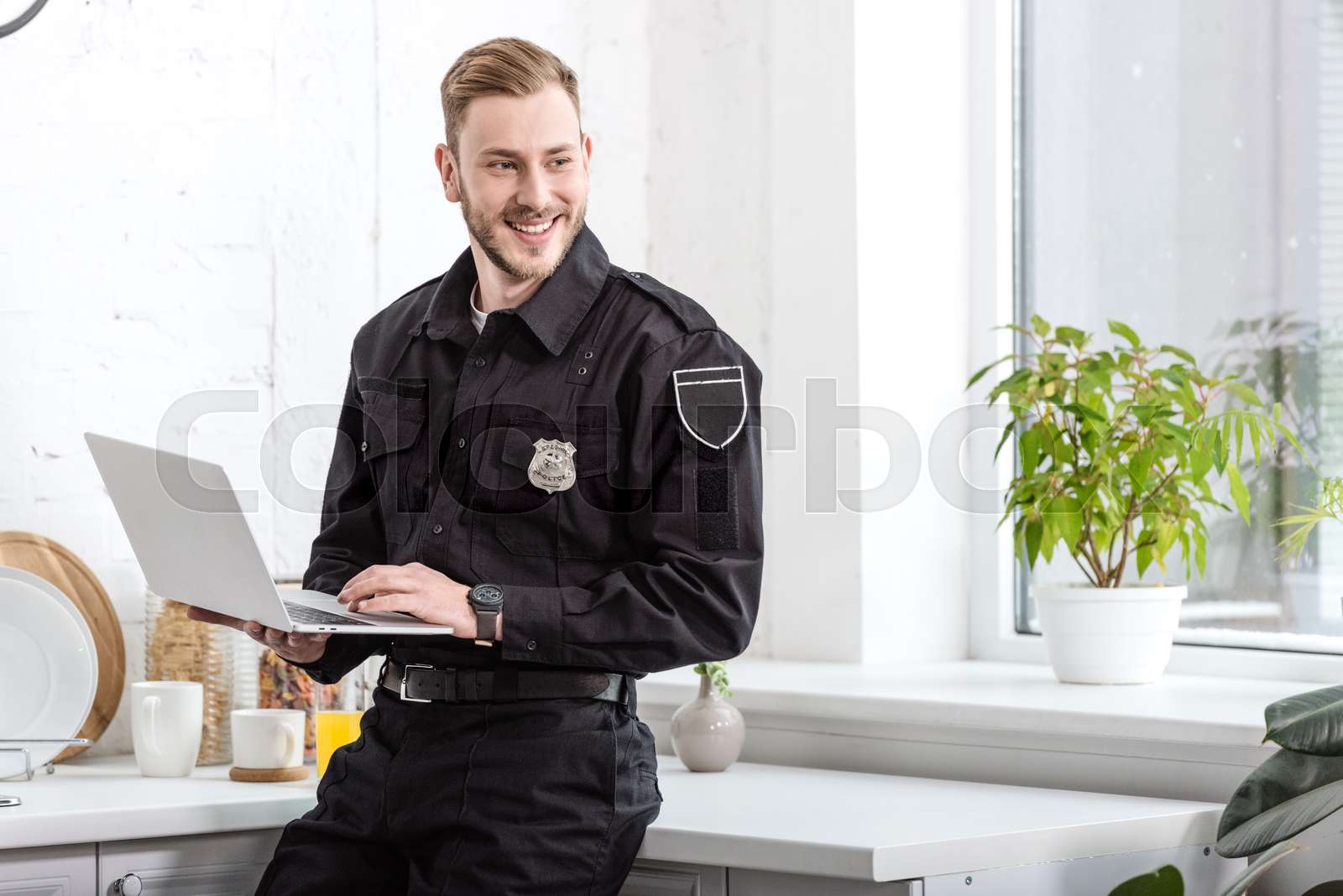 handsome policeman smiling and using laptop at kitchen | Stock image ...