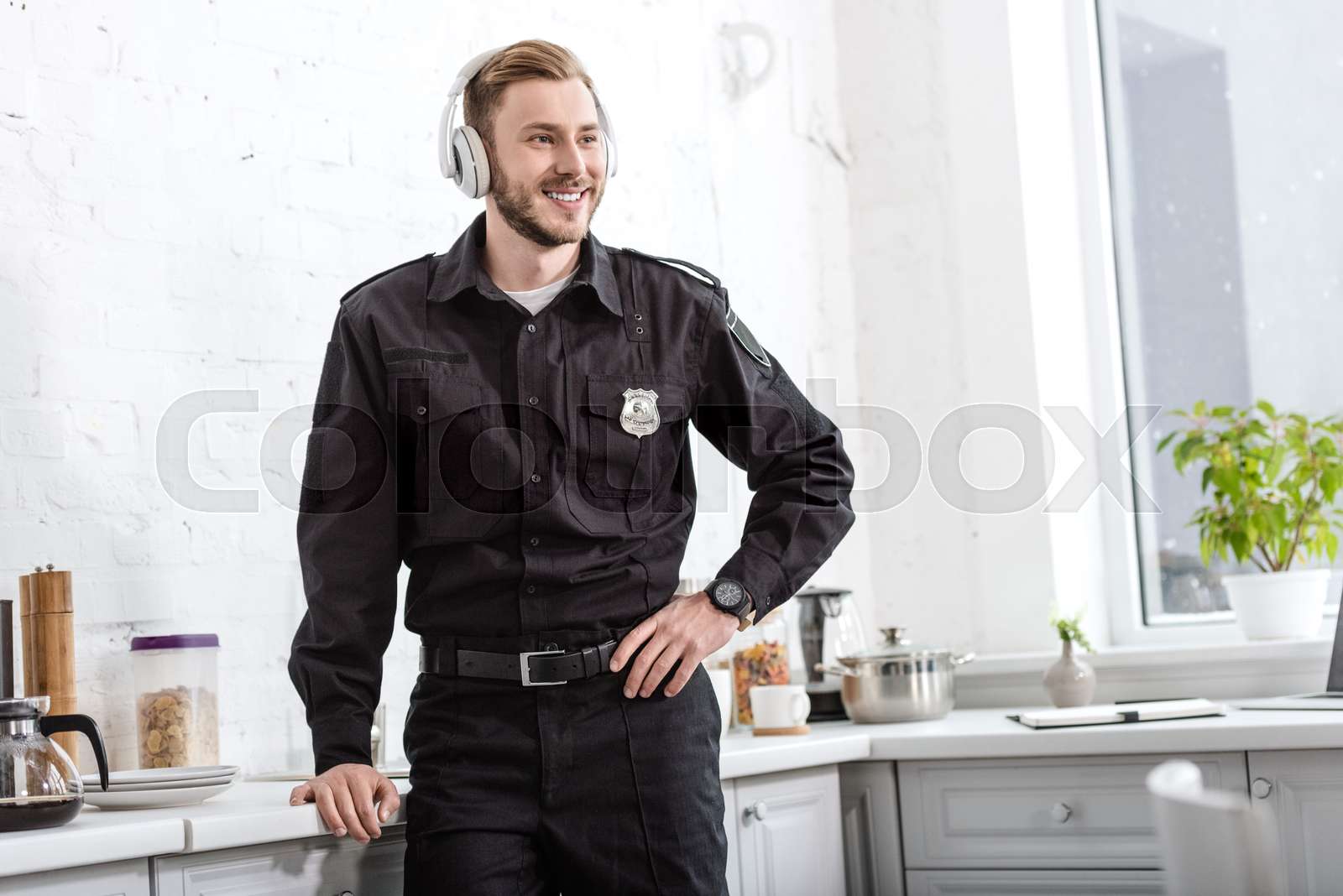 smiling police officer listening to music with headphones at kitchen ...