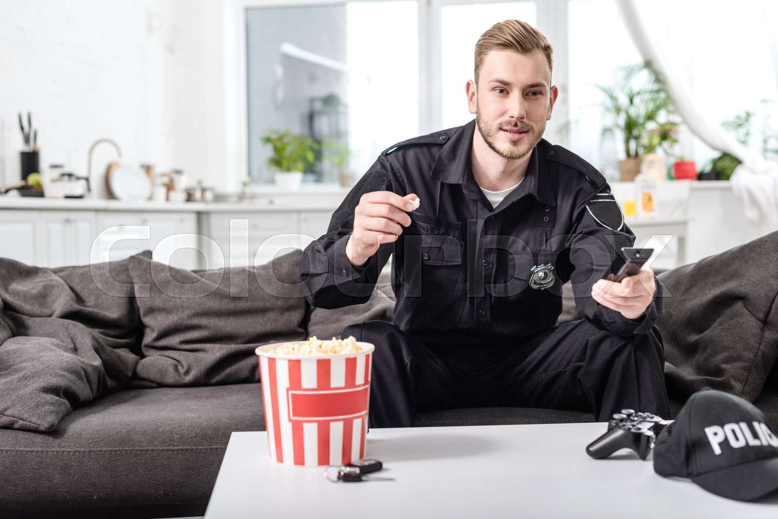 policeman sitting on couch, eating popcorn and watching movie | Stock ...