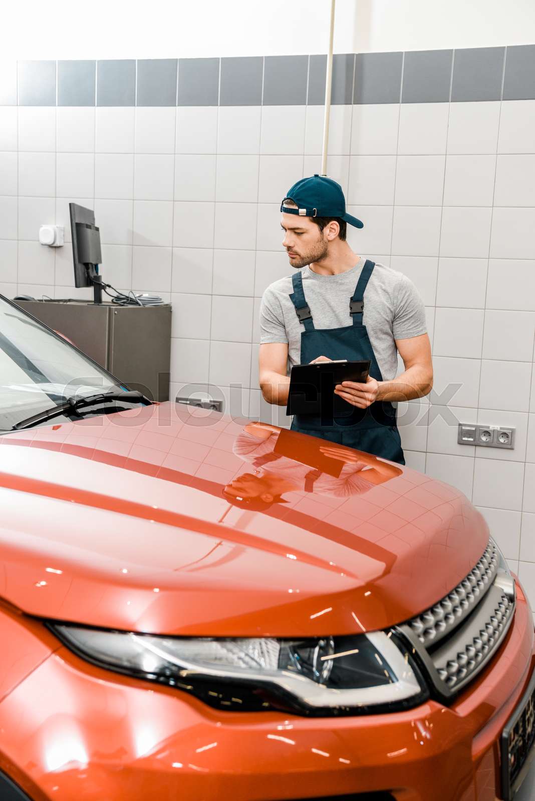 portrait of focused auto mechanic with notepad examining car at auto ...