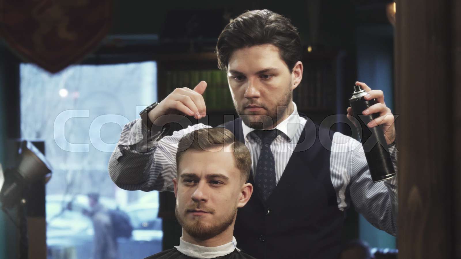 Professional barber using hairspray styling hair of a young man | Stock ...