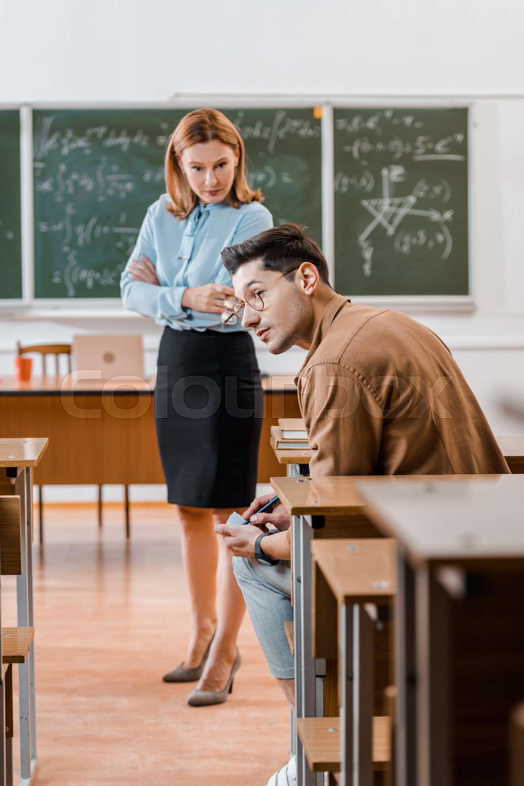 dissatisfied female teacher with arms crossed looking at male student ...