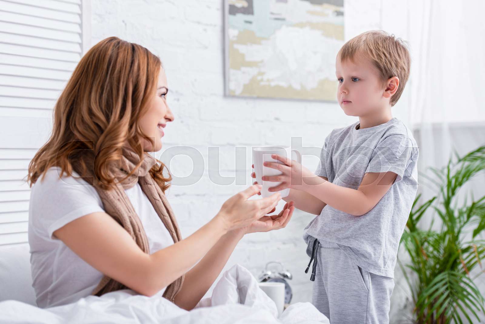 side view of son giving cup of tea to sick mother in bedroom | Stock ...