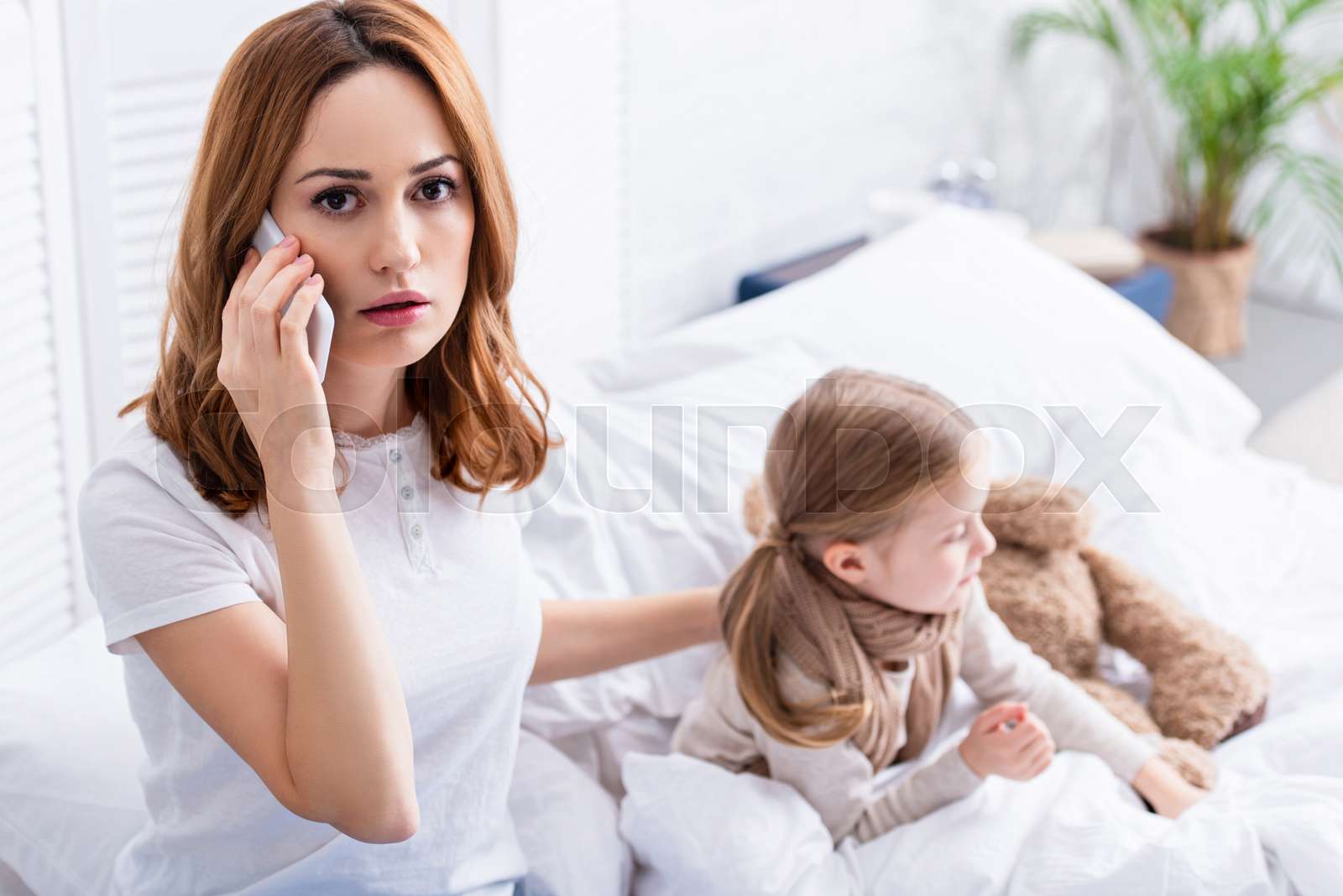 scared mother calling doctor by smartphone, sick daughter in bed ...