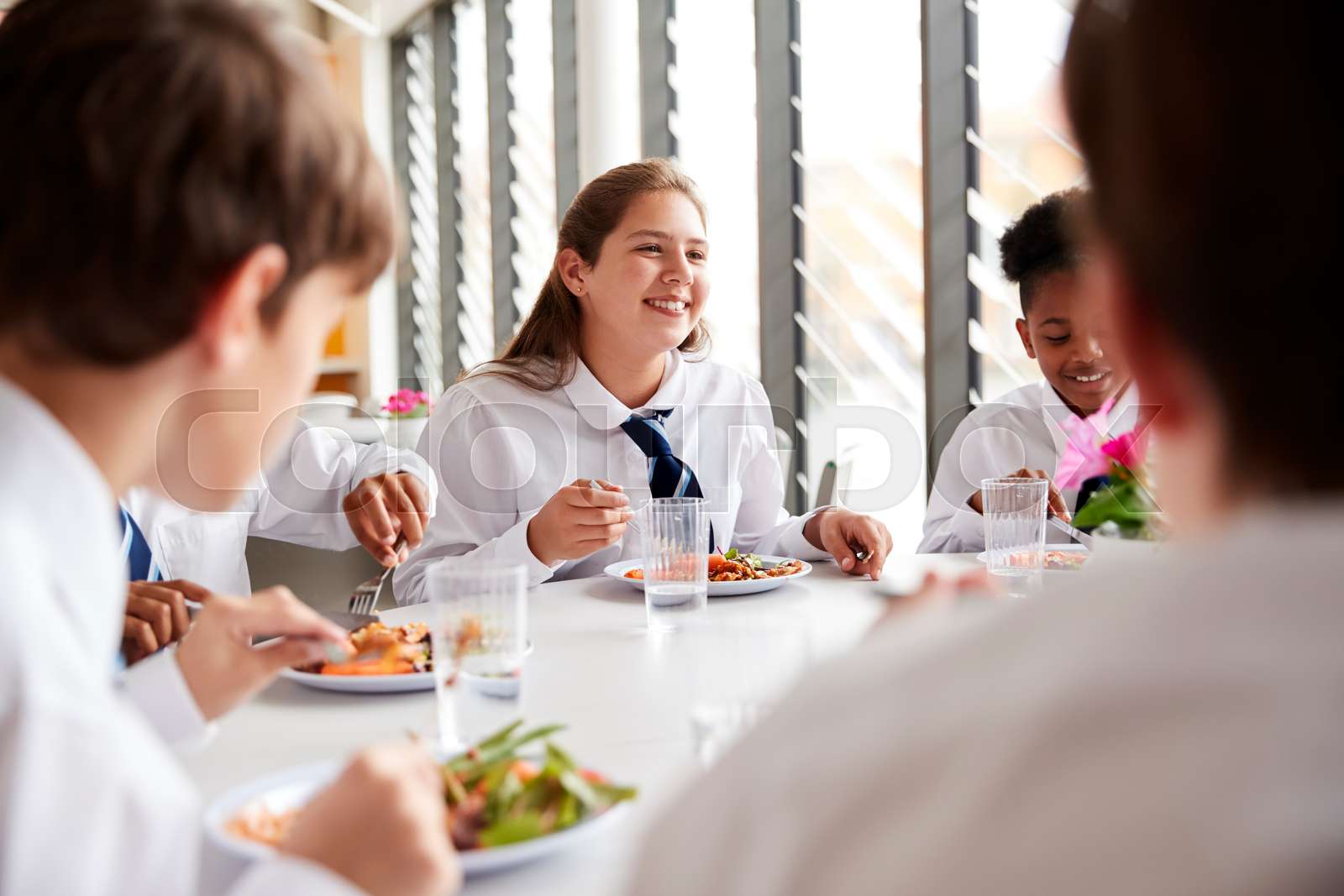 Group Of High School Students Wearing Uniform Sitting Around Table And ...