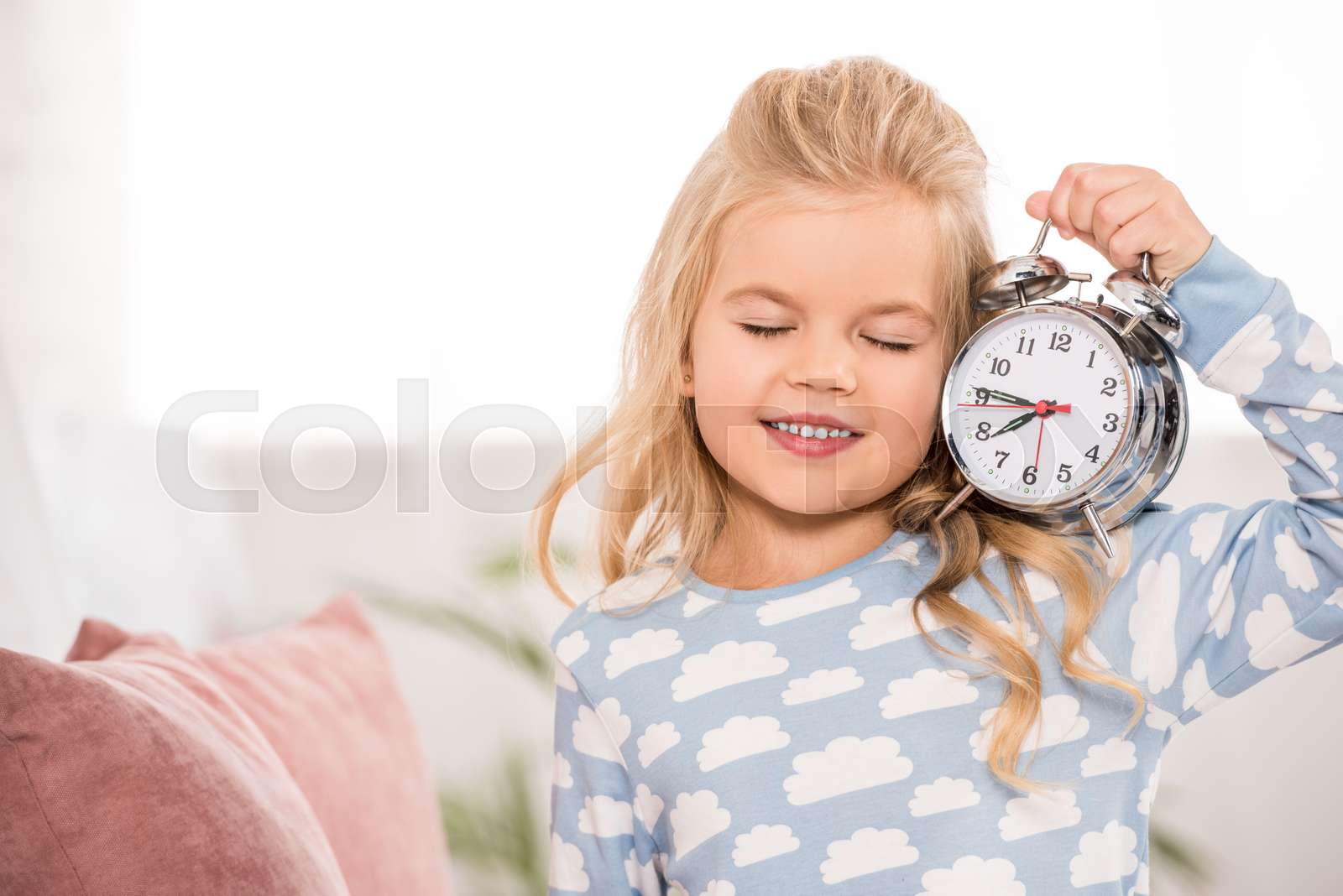 smiling adorable child with clock and closed eyes in bedroom | Stock ...