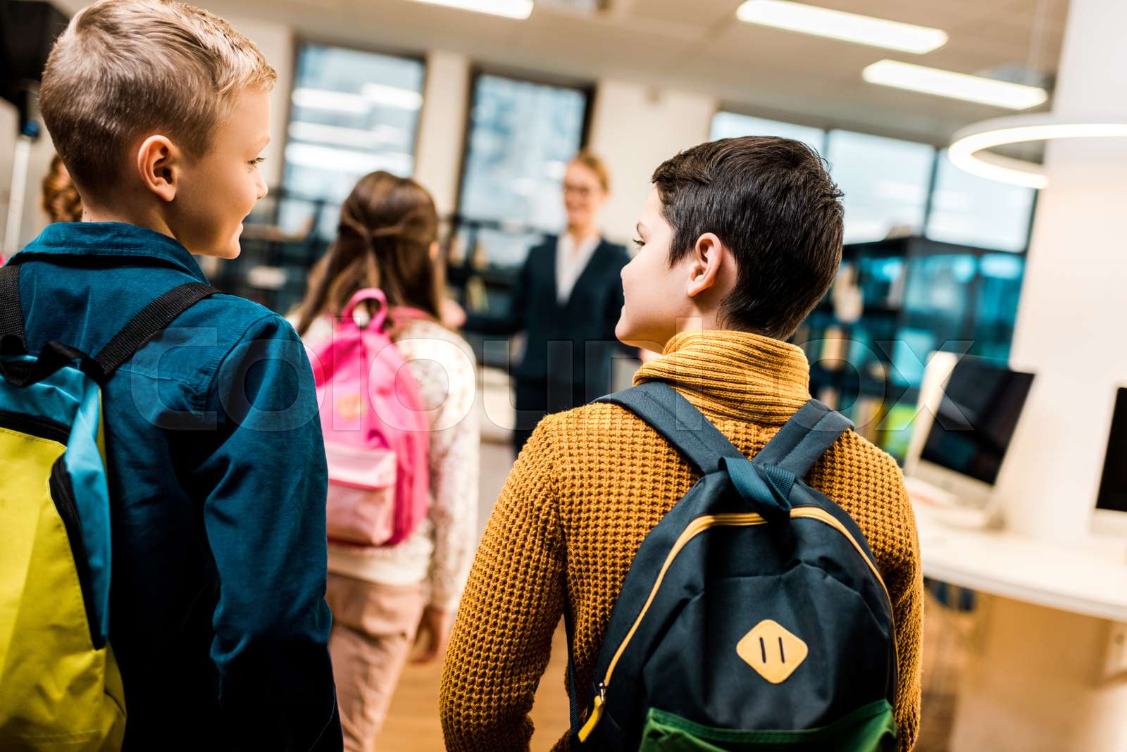 back view of boys with backpacks looking at each other while visiting ...