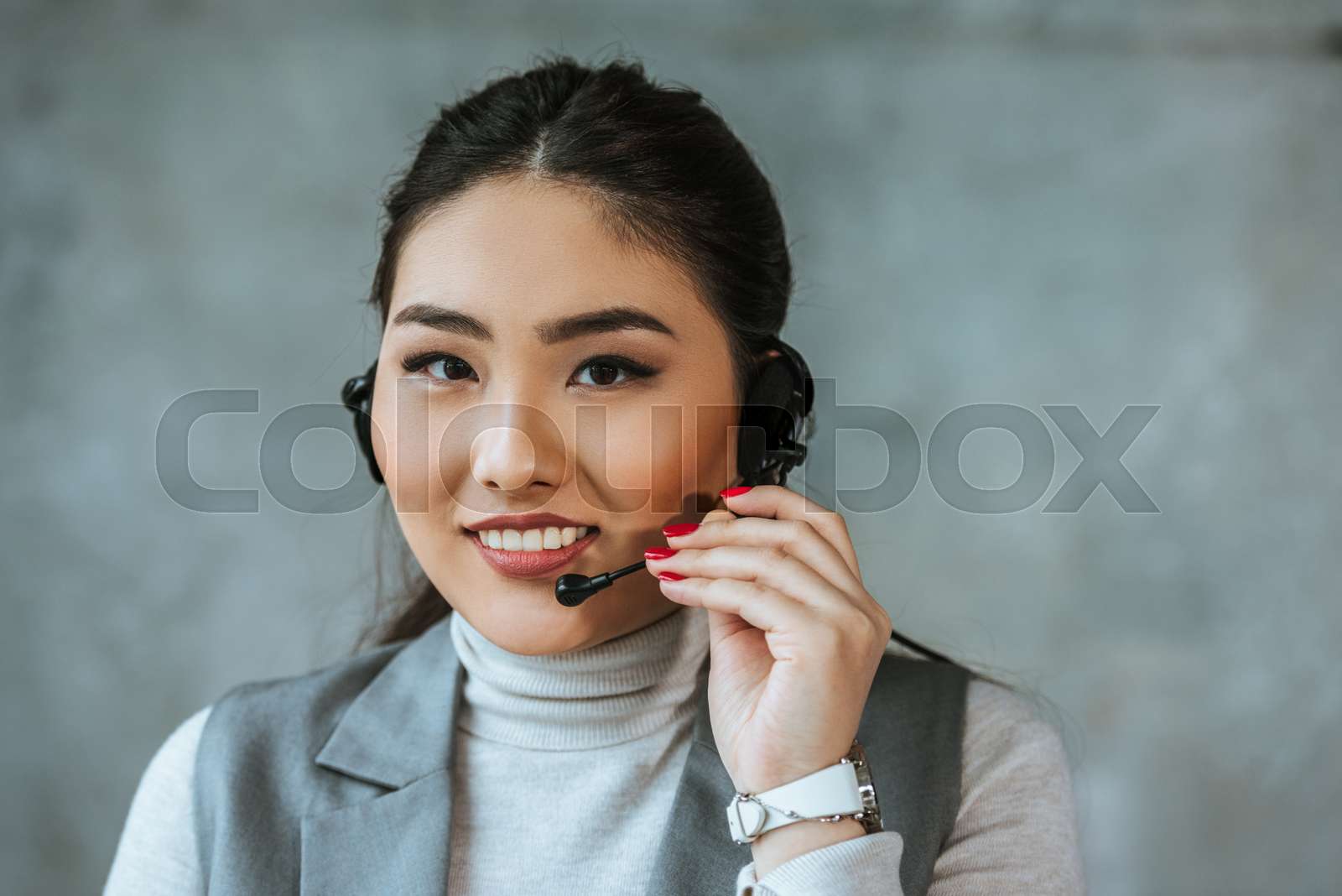 beautiful young asian call center operator smiling at camera on grey ...