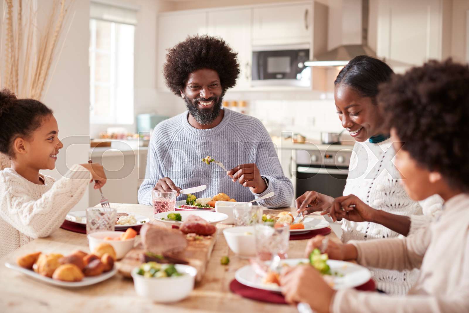Happy mixed race young family of four eating Sunday dinner together ...