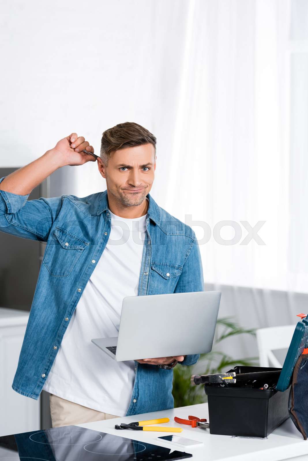 confused man holding laptop and scratching head with tool | Stock image ...