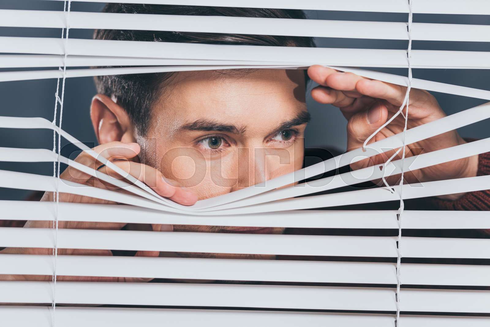 suspicious young man looking away through blinds, spying concept ...