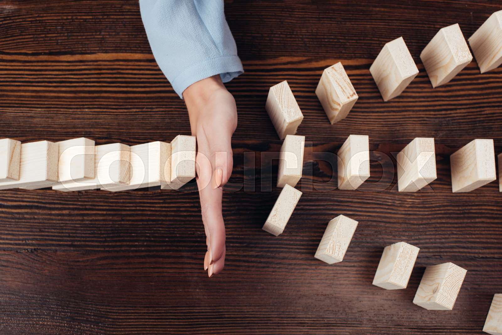 cropped view of woman preventing wooden blocks from falling at desk ...