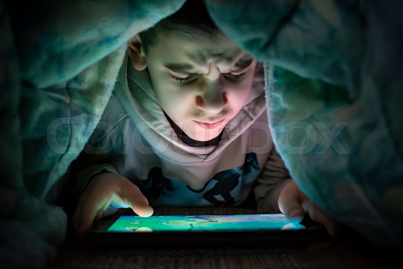 Child watching his tablet in the bed. Illuminated child face from ...