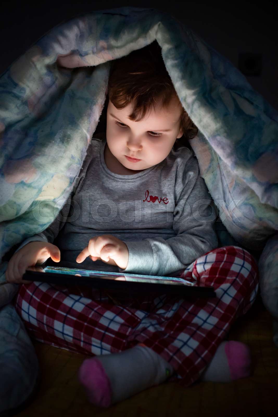 Little girl watching her tablet in the bed. Illuminated child face from ...