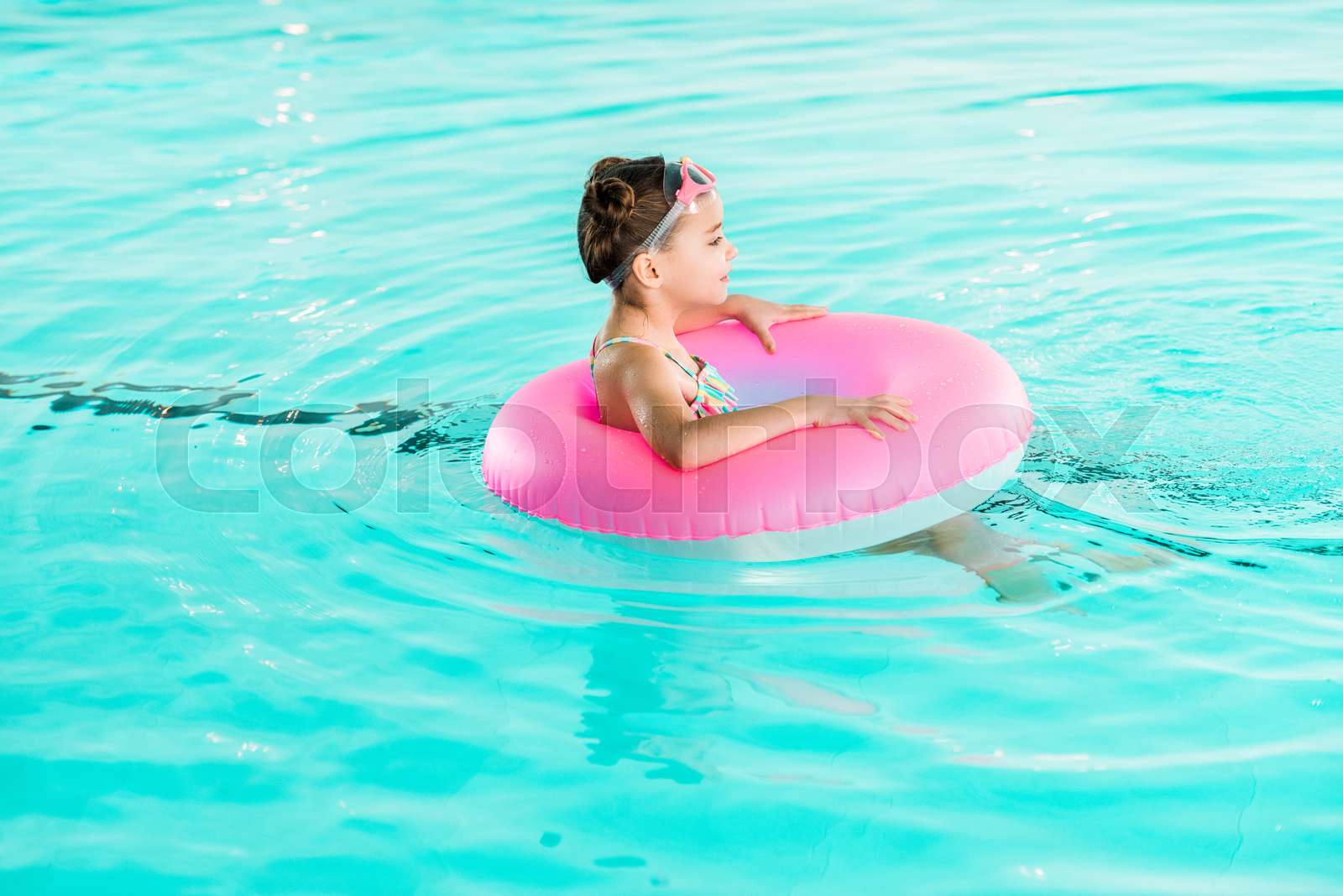 child in googles learning swimming with inflatable ring in swimming ...