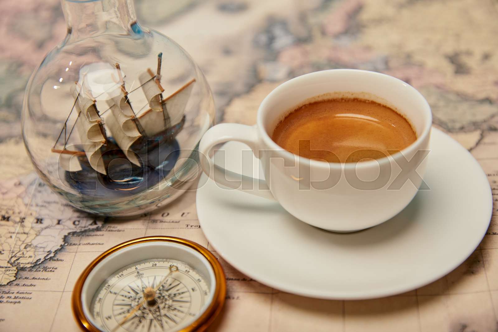 coffee cup, compass and toy ship in glass bottle on world map | Stock ...