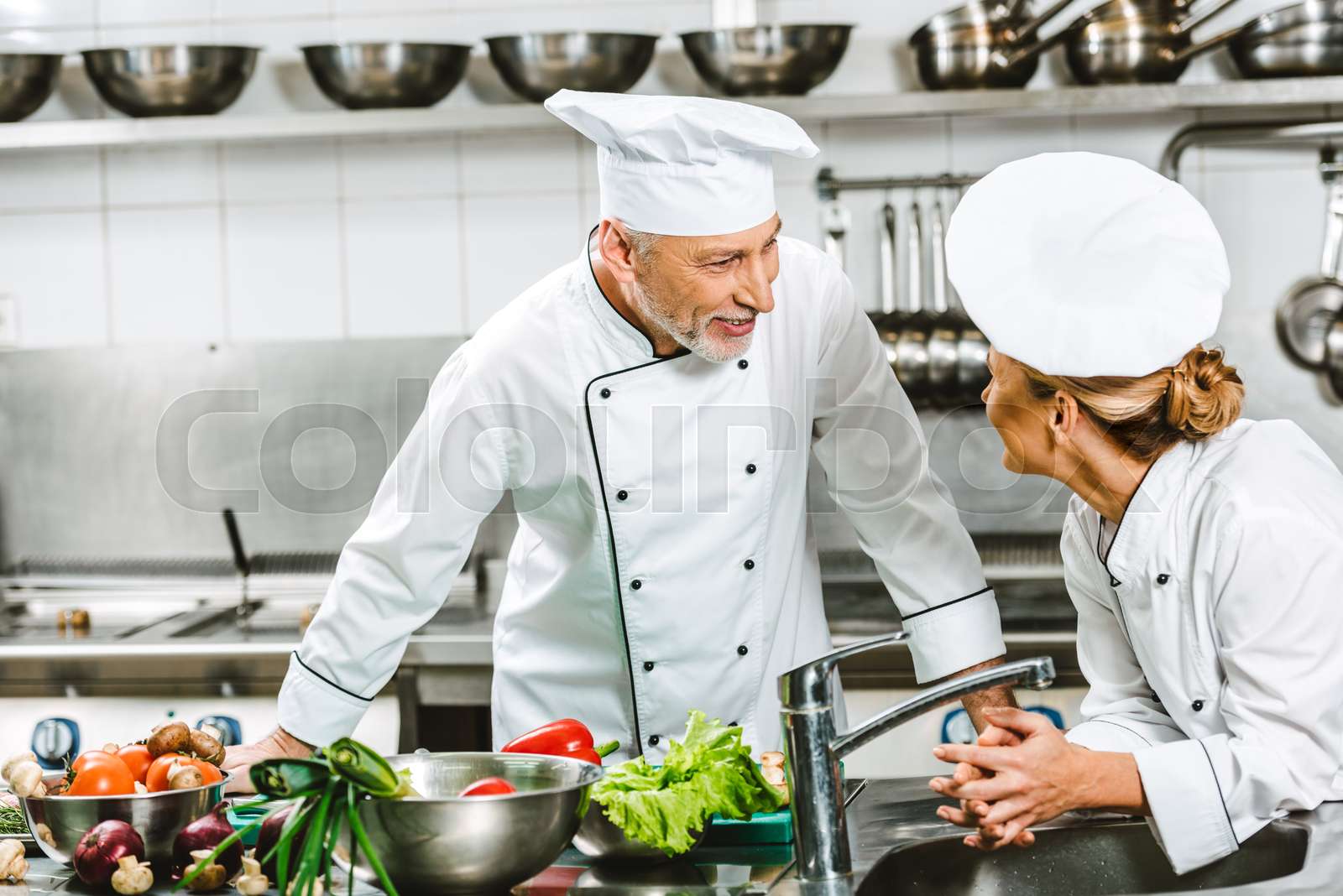 female and male chefs in uniform looking at each other while cooking in ...