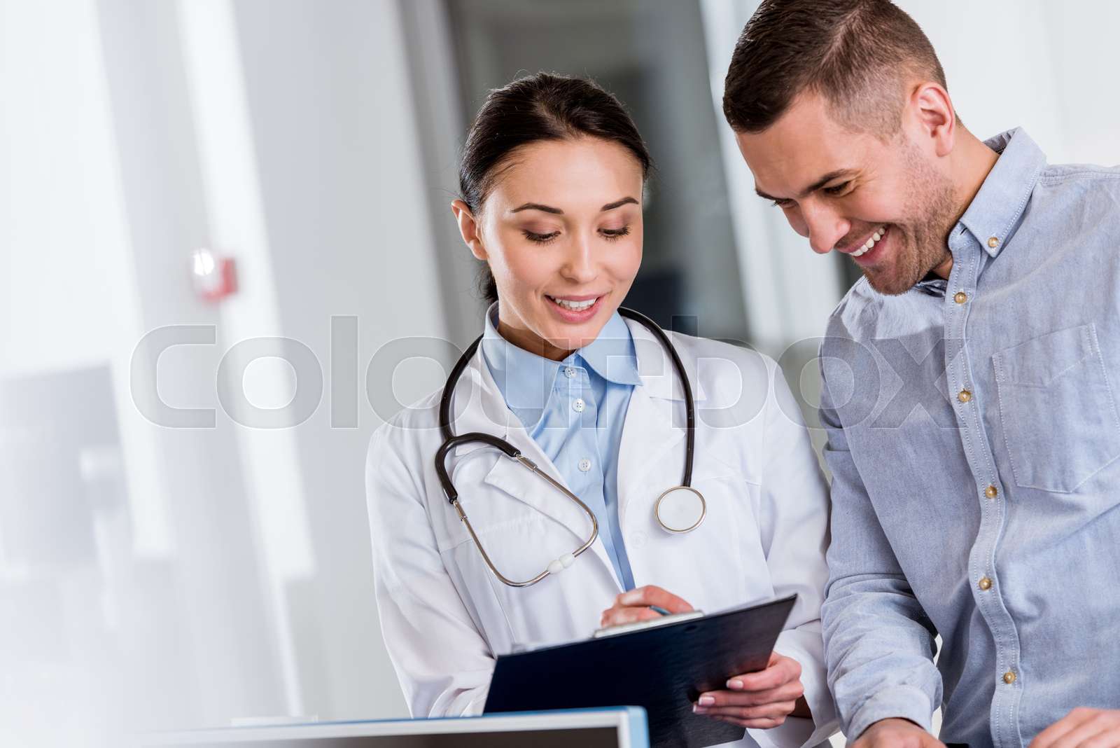 Laughing doctor talking to patient and writing in clipboard | Stock ...