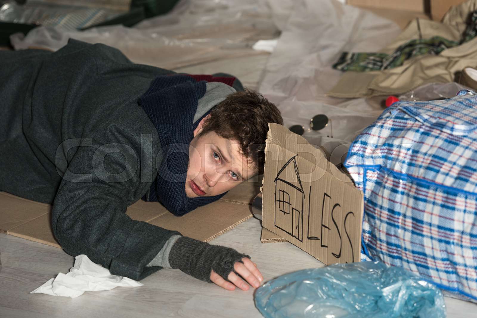despaired homeless man lying on cardboard in rubbish dump, with symbol ...