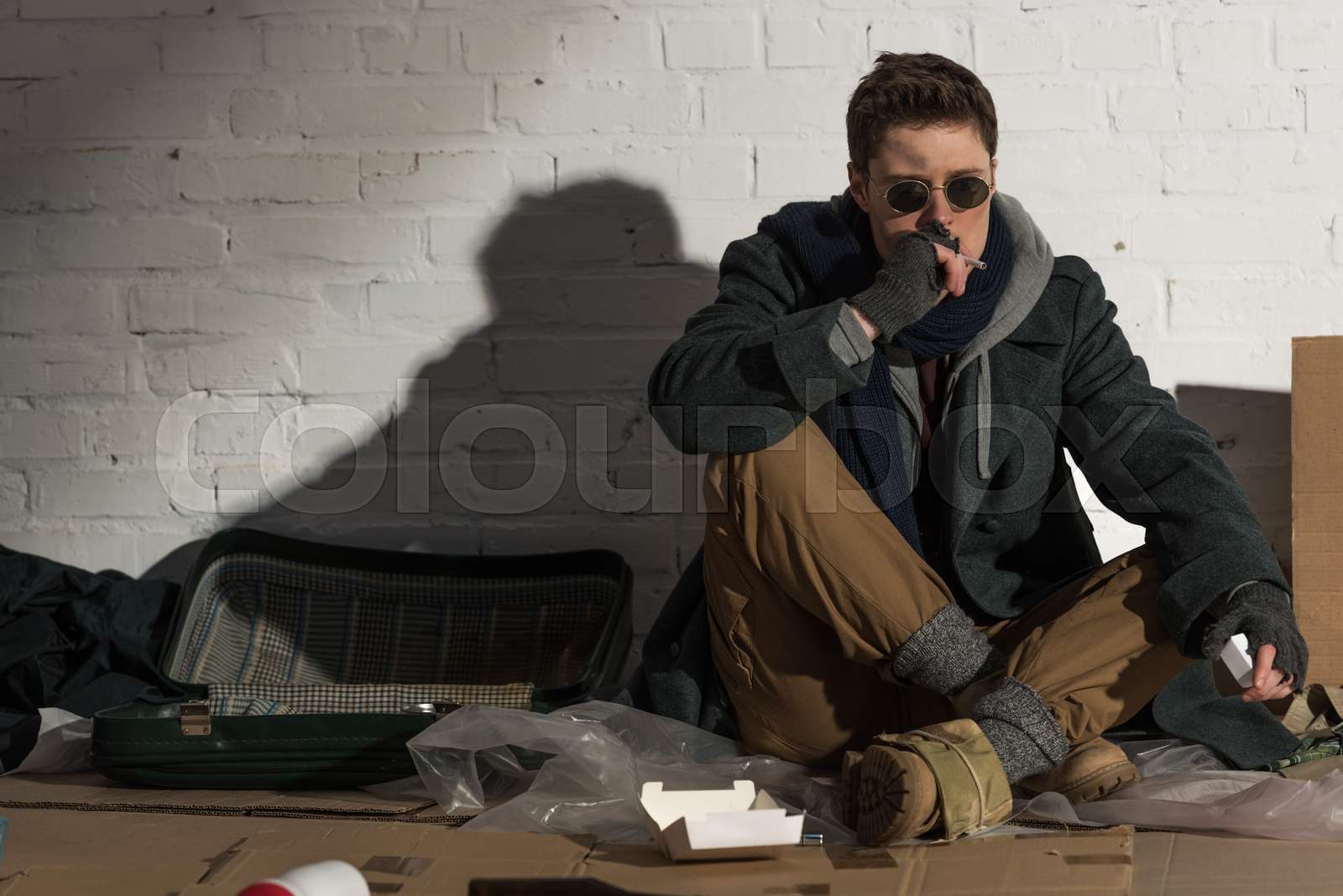 homeless man smoking cigarette while sitting on rubbish dump | Stock ...